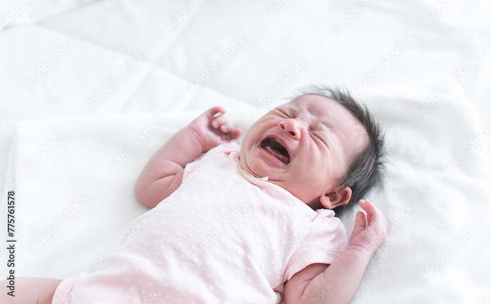 Newborn baby girl crying and screaming, lying on bed at home. Asian ...