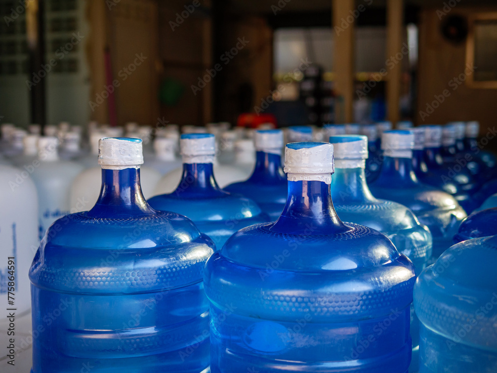 Many blue gallons and white gallon of drinking water are lined up in a ...