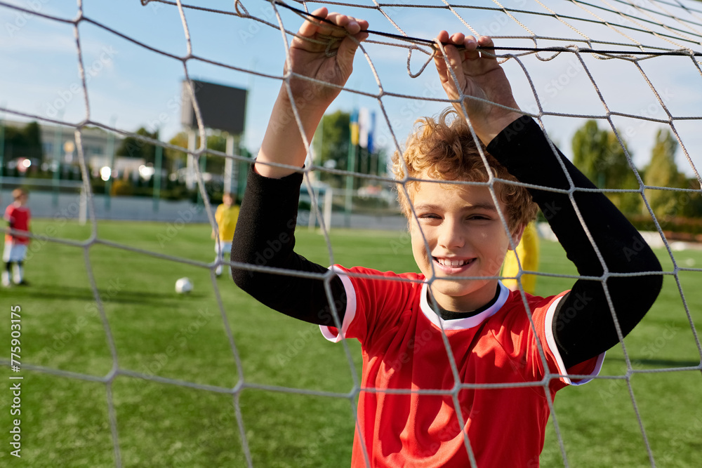 A young boy stands confidently in front of a soccer goal, focused on ...