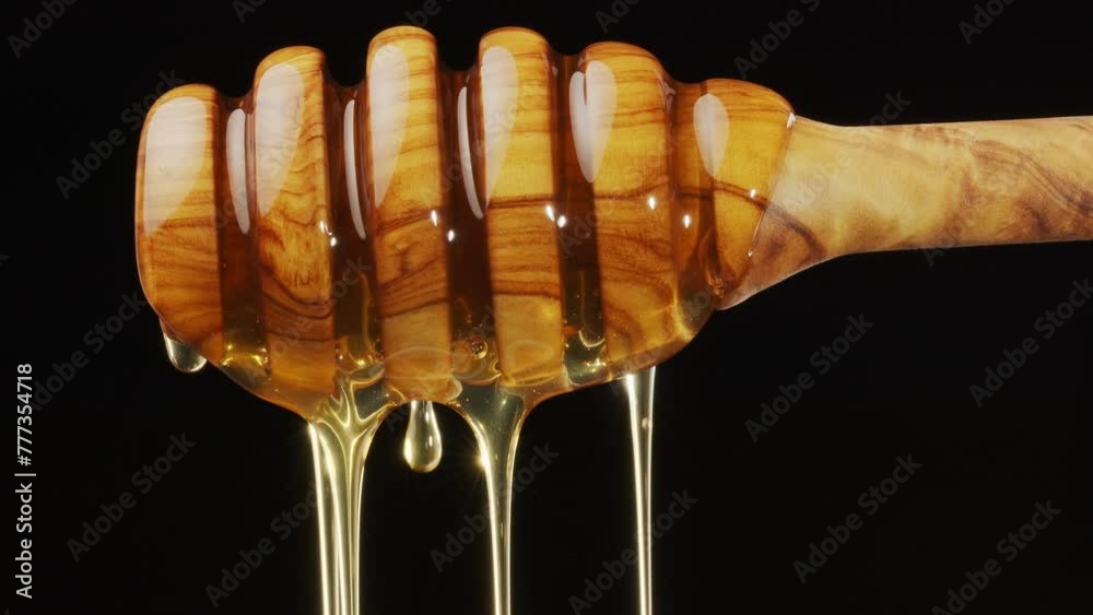Drops of honey flow from a wooden honey dipper and slowly drip down ...