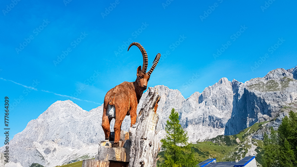 Statue of wooden goat with panoramic view of mountain peak Dachstein in ...