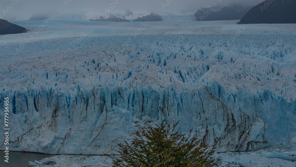 A mass of blue ice with cracks, crevices, and sharp peaks stretches to ...