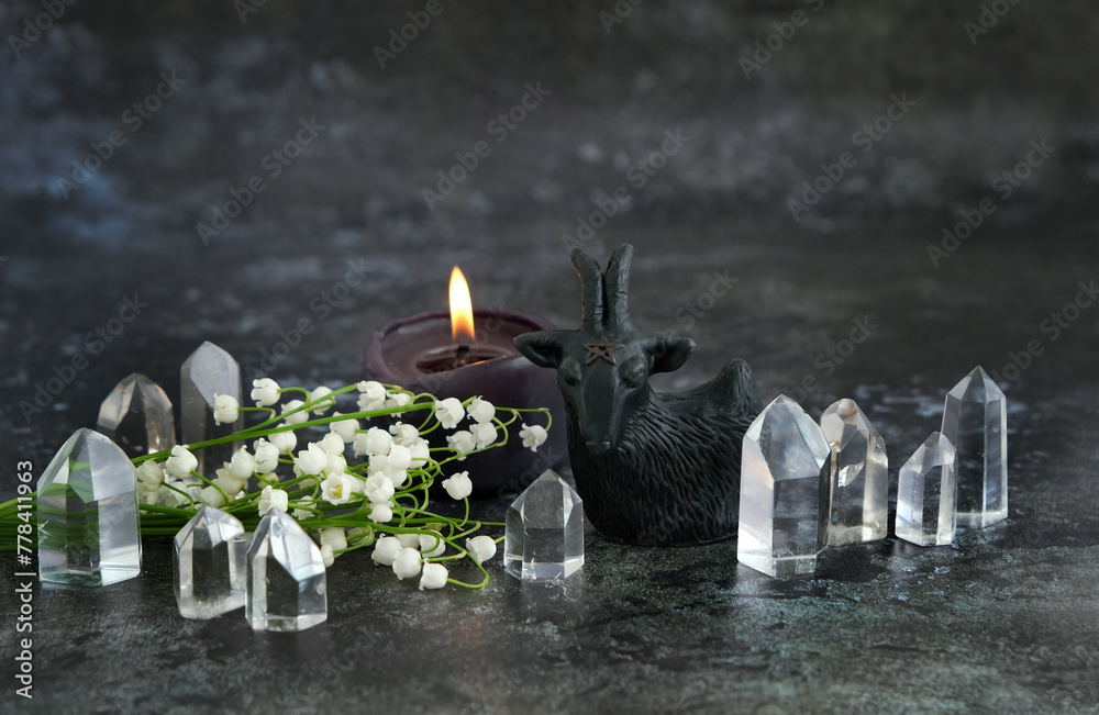 amulet in goat form, candle, crystals and flowers on table, dark ...