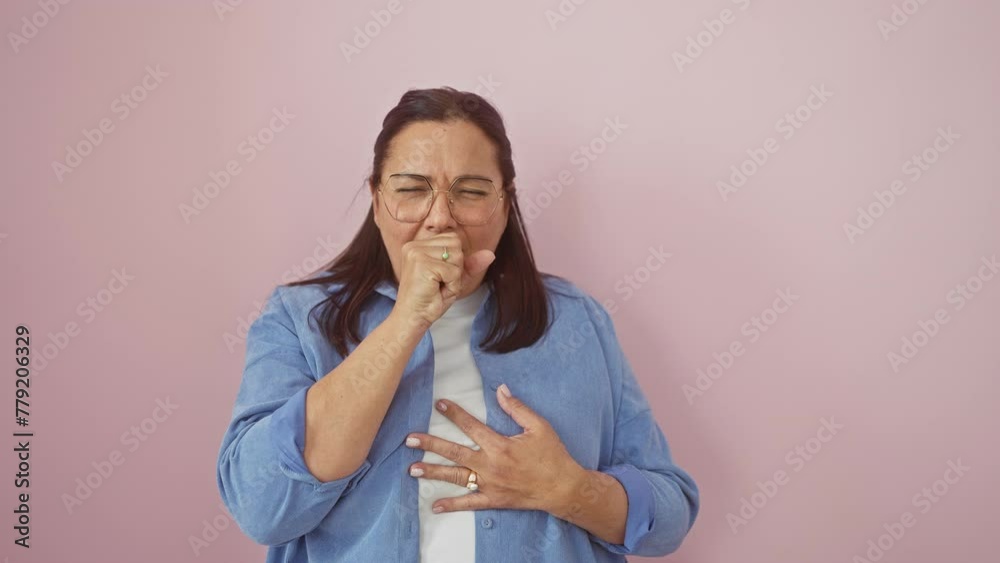 Unwell middle age hispanic woman in glasses coughing over pink isolated ...