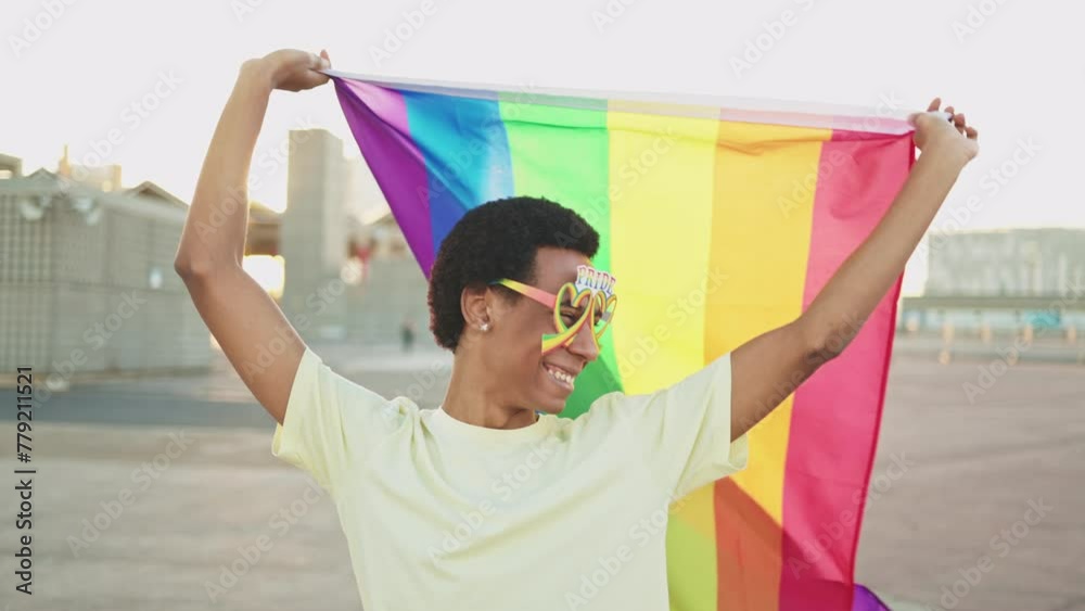 Cheerful African American gay man dancing with rainbow LGBT flag at ...