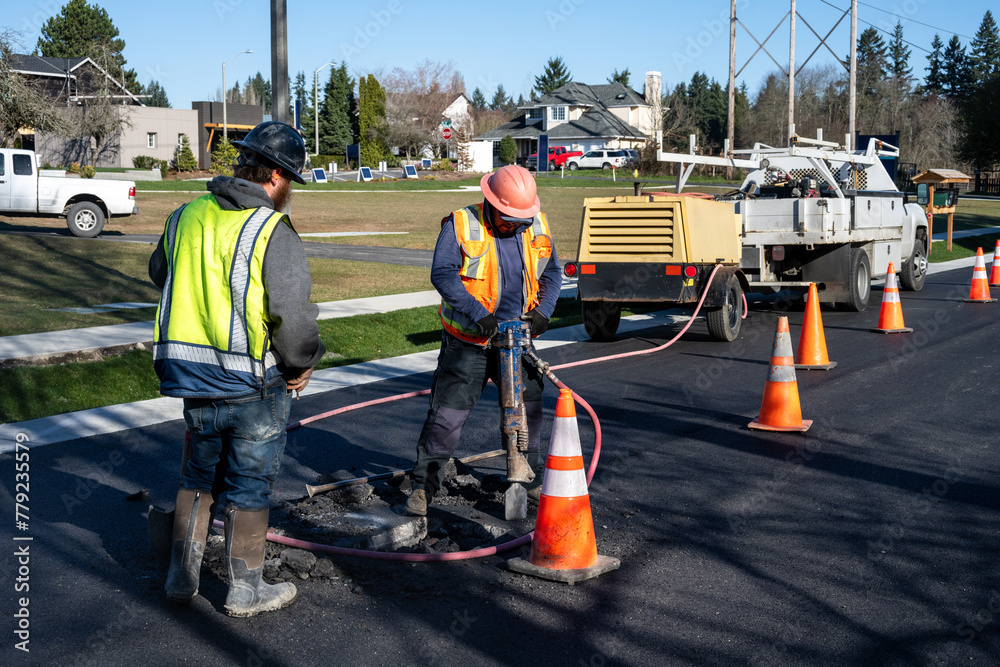 Construction workers using a jackhammer to dig up freshly laid asphalt ...