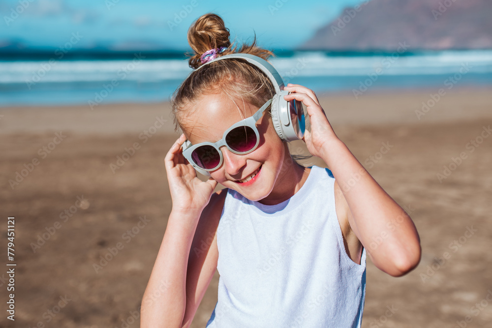 Girl with headphones on head, on beach. Smilling blonde girl enjoying ...