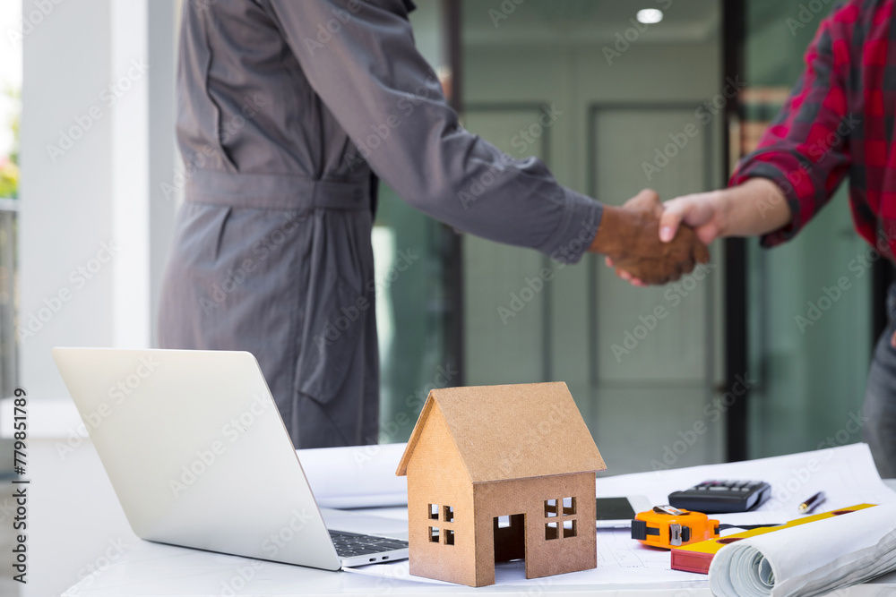 House model on desk over architect and engineer or contractor shaking ...