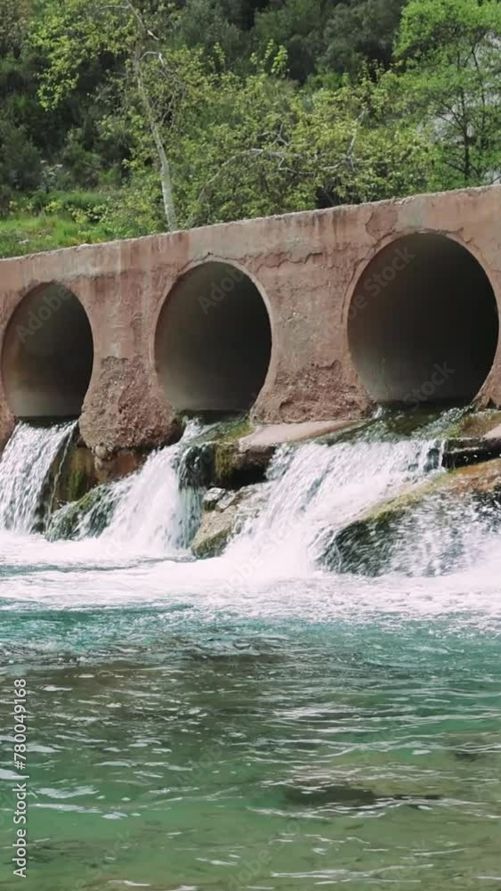 Captivating view of a bridge, dam over a small river with vibrant green ...