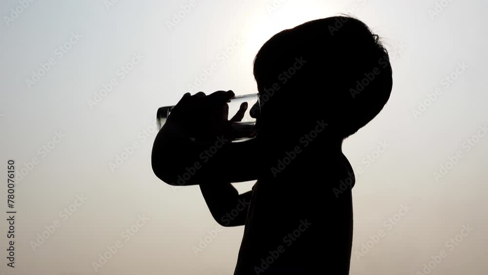 A thirsty kid drinks water from a transparent drinking glass in the hot ...