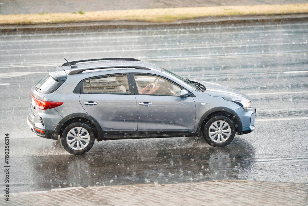 Car driving through the rain on city road - handling wet roads, puddles, and hail safely. Car ...