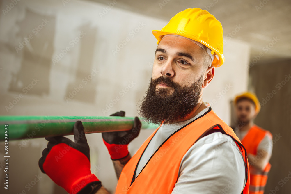 Two construction workers carrying pipes at a building site - people at ...