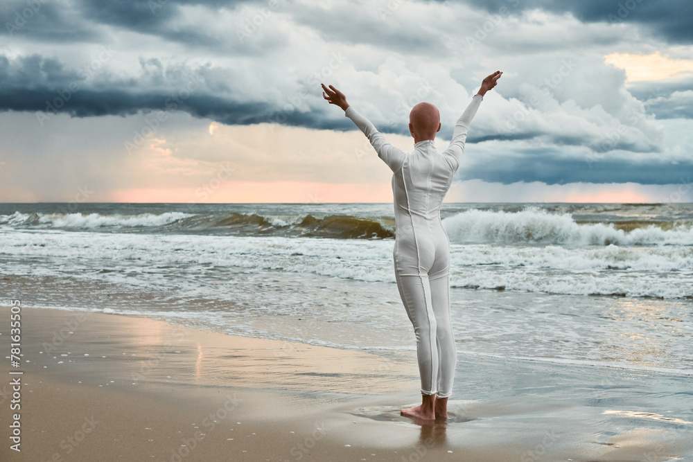Hairless girl with alopecia in white futuristic suit standing on sea ...
