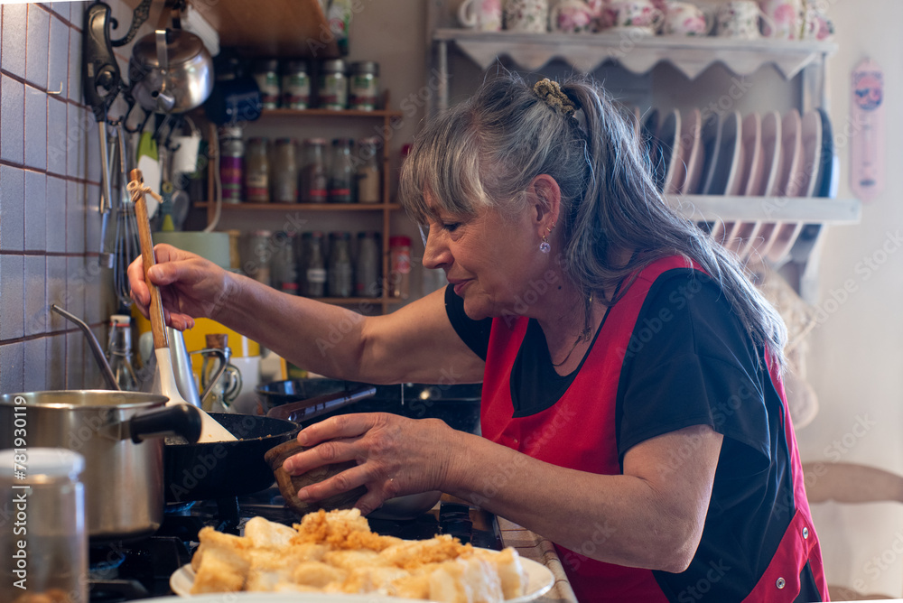 Woman in her sixties with long grey hair tied in a ponytail frying cod ...