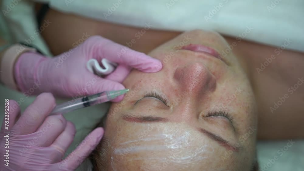 A woman is getting a facial treatment with a syringe. The woman is ...