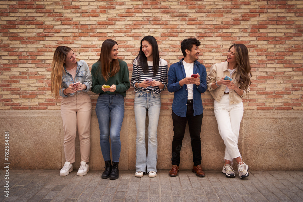 Group diverse happy young friends leaning on brick wall looking at each ...