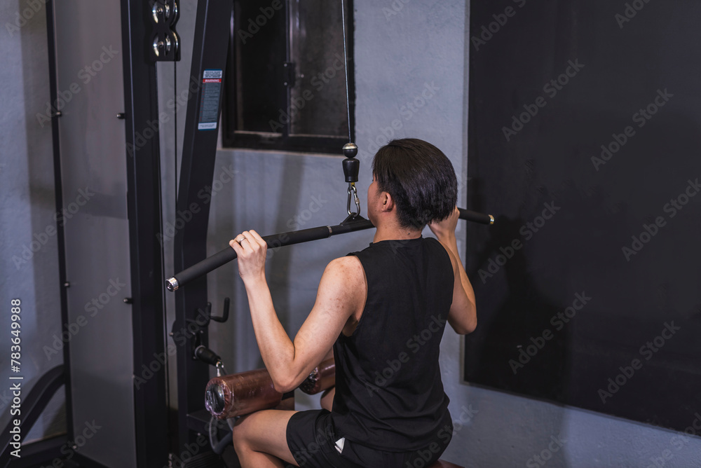 A skinny and lanky young man does a set of lat pulldowns to build back ...