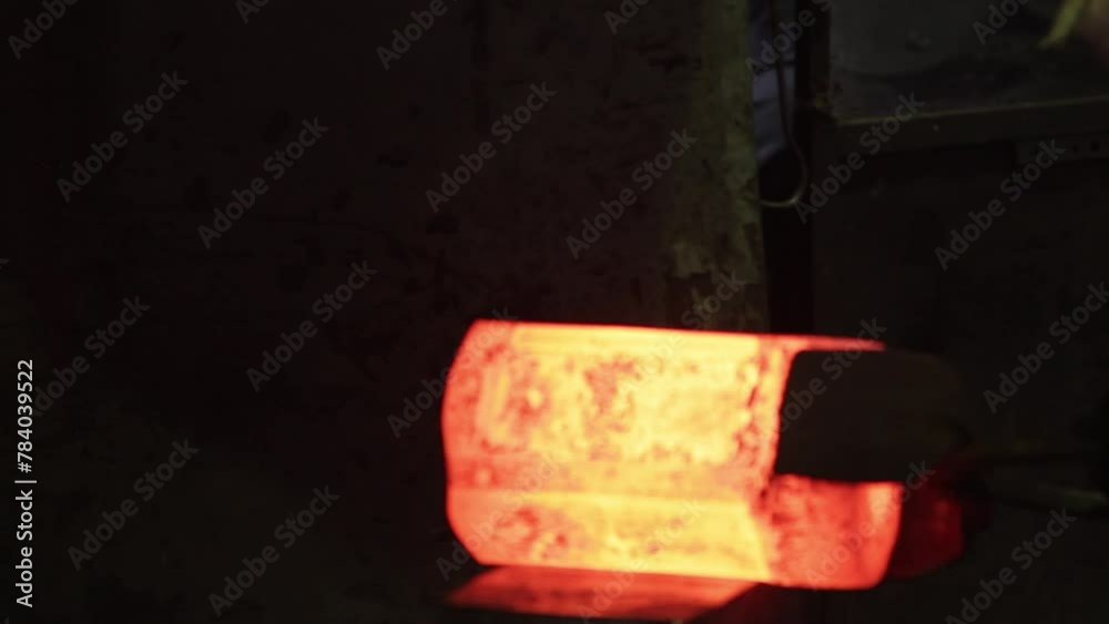Industrial worker manipulates glowing metal billet in forge, hammering ...