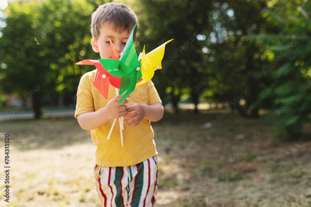 A 3-4 year old boy hides his eyes behind colorful pinwheels. The child ...