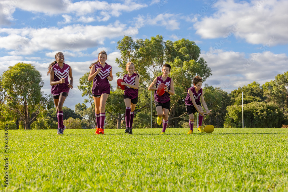 five children in football uniforms running towards the camera on green ...