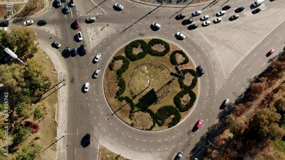 An aerial view of an urban design roundabout with cars driving around it, surrounded by asphalt ...
