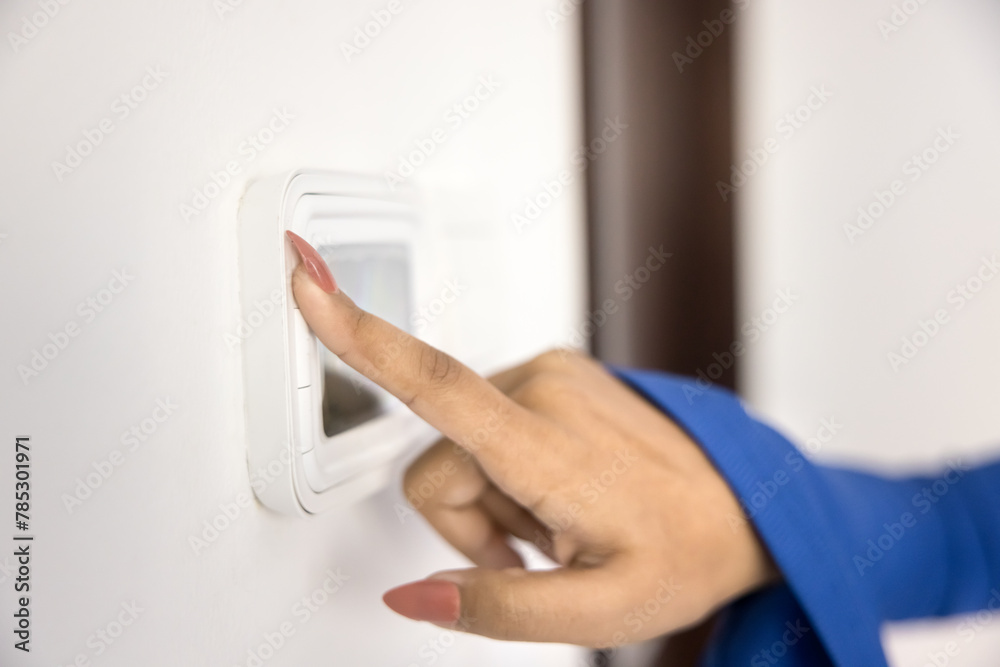 Young woman using climate control panel at home, regulating thermostat ...