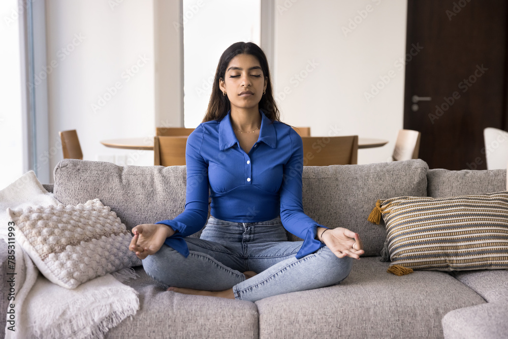 Focused tranquil young Indian yogi girl meditating at home, sitting on ...