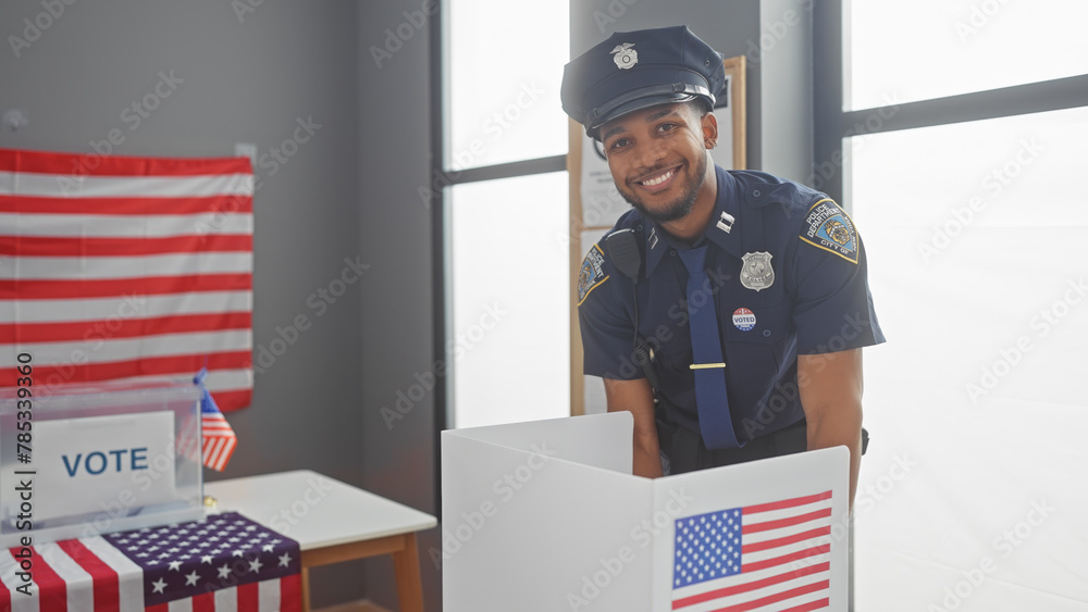 A smiling african american male police officer stands by a voting booth ...
