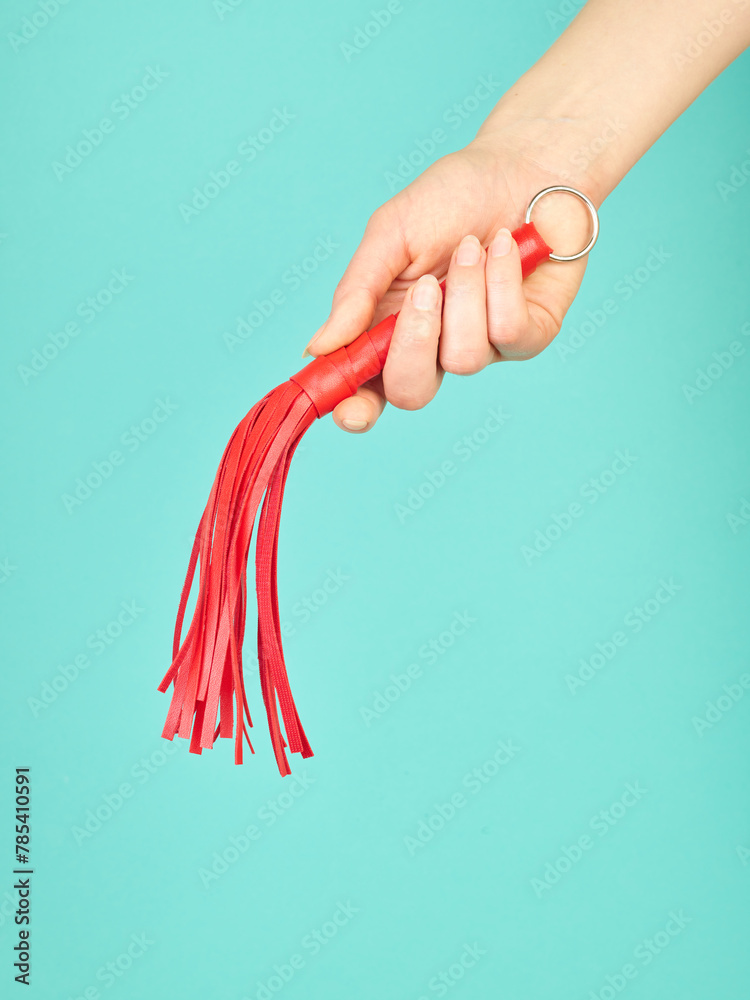 Red whip for adult role play games in woman's hand over turquoise blue ...
