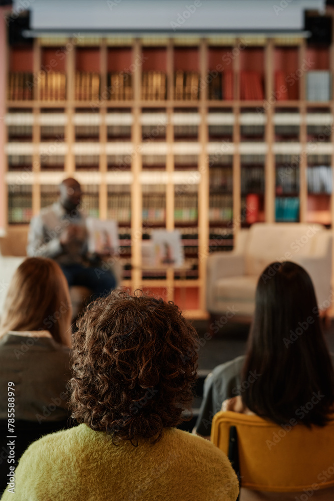 rear view of several female readers sitting in rows in front of stage ...