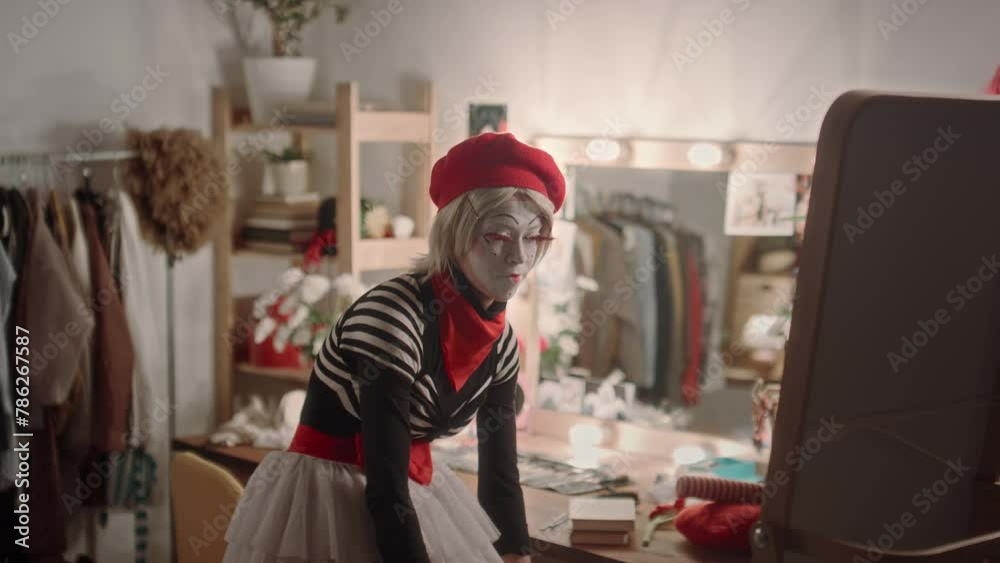 Female mime artist with stage makeup putting on costume, looking in ...