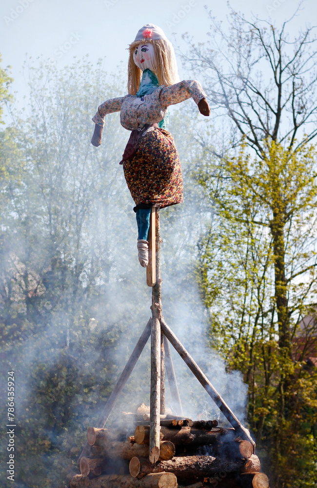 A funny dummy of a witch attached to a wooden cross on a bonfire with smoke rising from it on ...