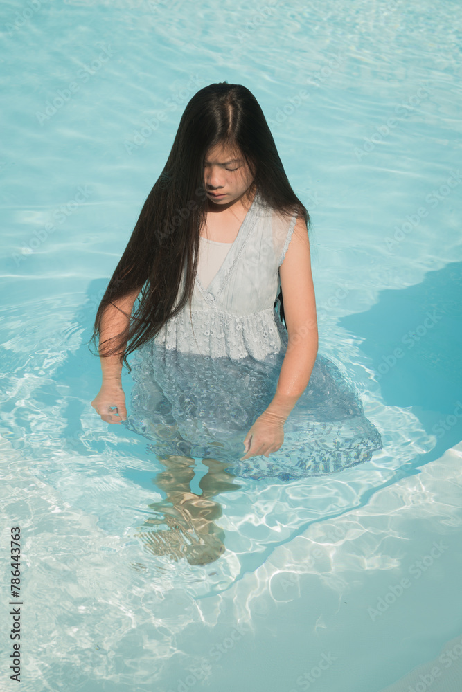 art portrait of girl in blue dress wading in swimming pool in summer ...