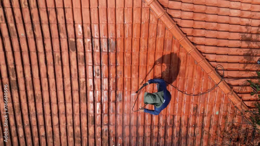 A person outdoors cleaning the red clay roof using a high pressure ...