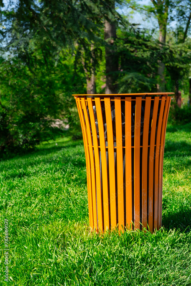 Trash can stands in a green park. A colored garbage bin in the grass ...