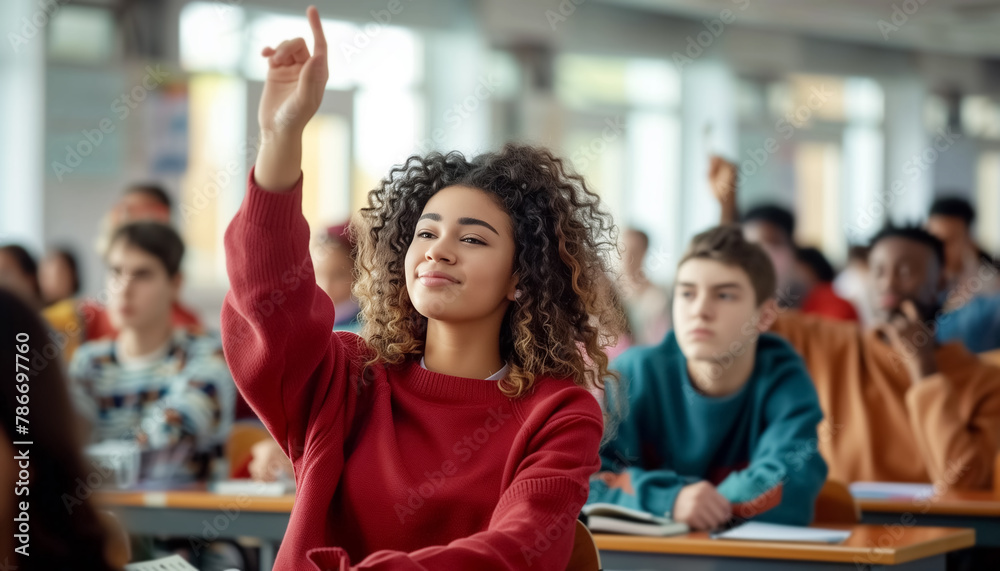 Curly teenage girl raises hand in classroom full of students. She looks ...