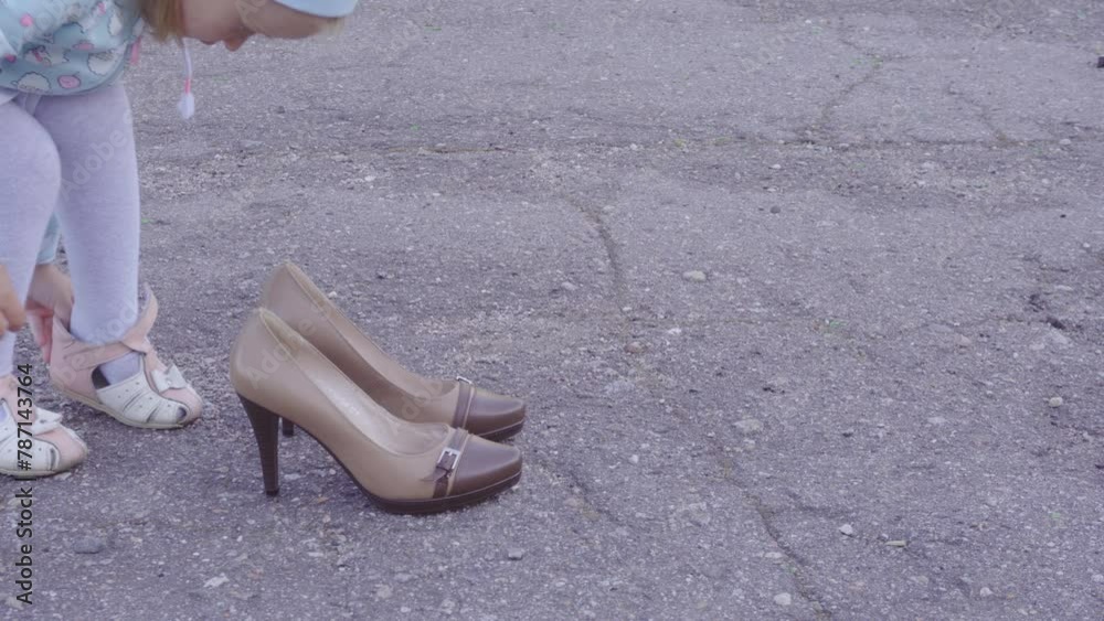 Little girl tries to take off her sandals and put on her mother's shoes ...