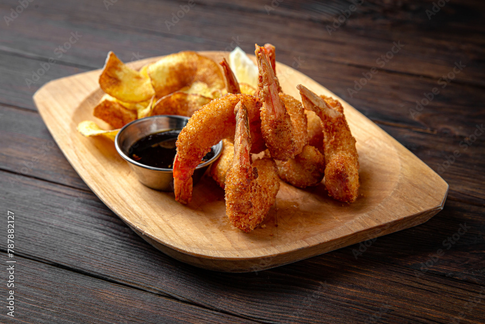 Battered king prawns with barbecue sauce and potato chips on dark ...