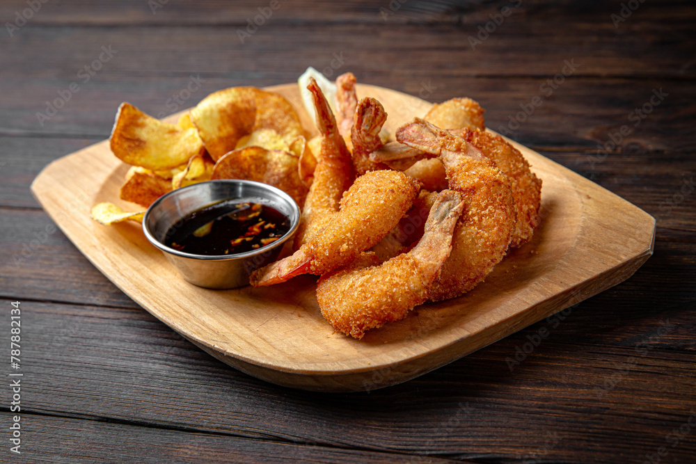 Battered king prawns with barbecue sauce and potato chips on dark ...