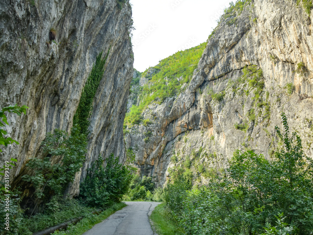An asphalt road winding in a narrow canyon sided by vertical, abrupt ...