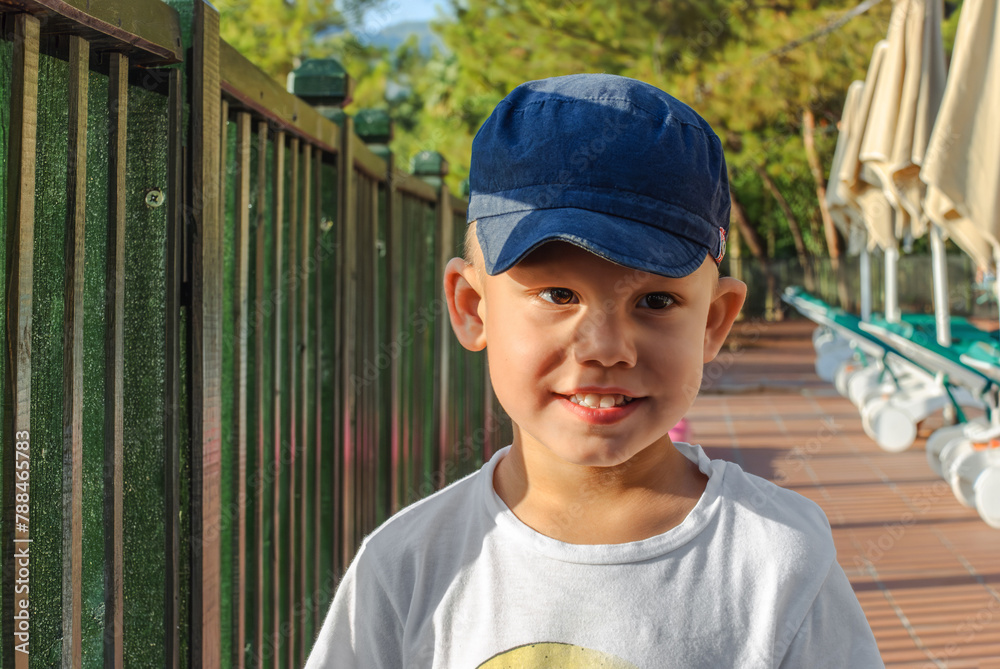 Cute little boy in a cap poses casually amid the coastal hotel sun ...