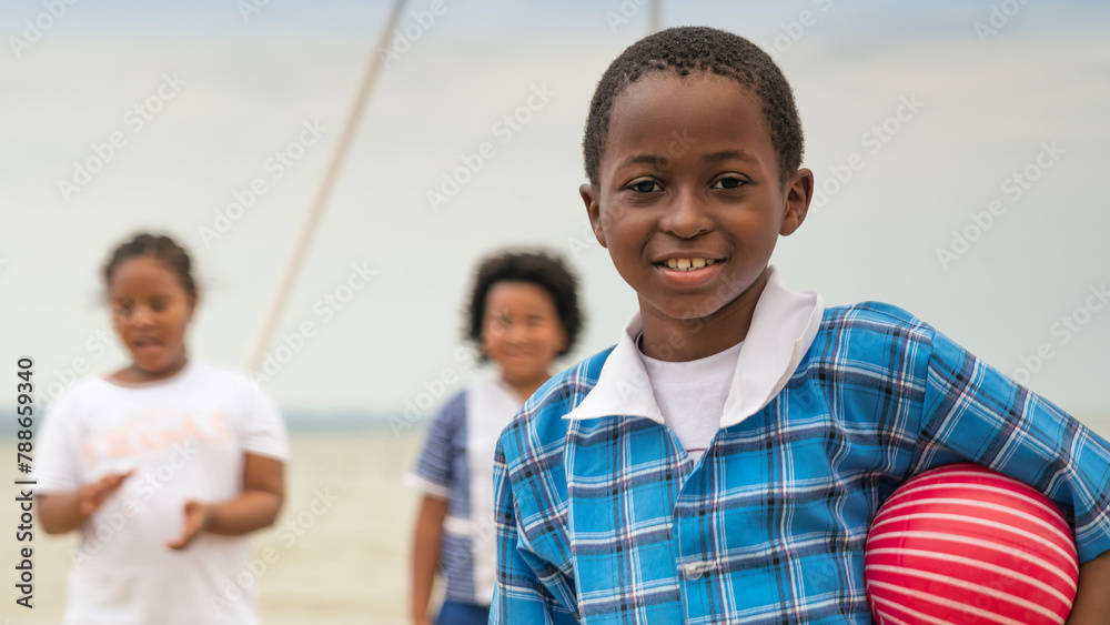 Portrait of a Garífuna boy on the beach, holding a red plastic ball ...
