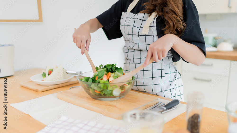 Young asian woman mixing fresh salad vegetables in glass bowl with ...