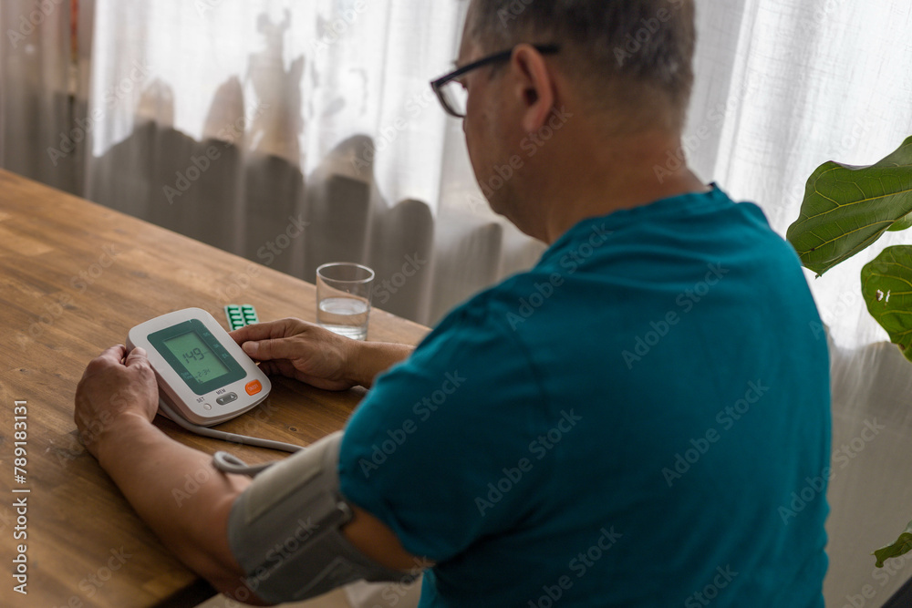 Seniory man checks blood pressure with monitor on upper arm in room ...