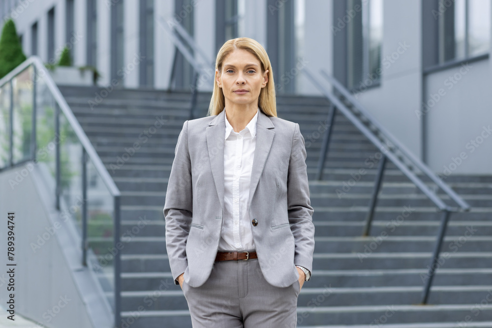 Focused female executive in a stylish gray suit stands on office ...
