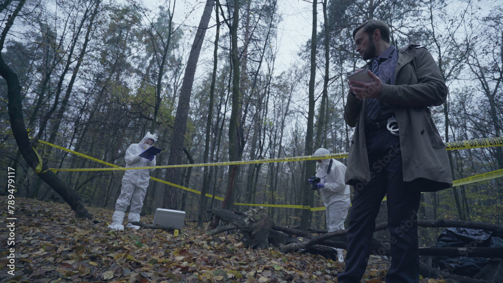 Police detective taking notes at a forest crime scene marked with ...