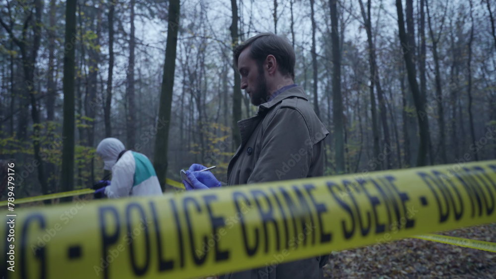 Busy investigator makes notes while a forensic expert collects evidence ...