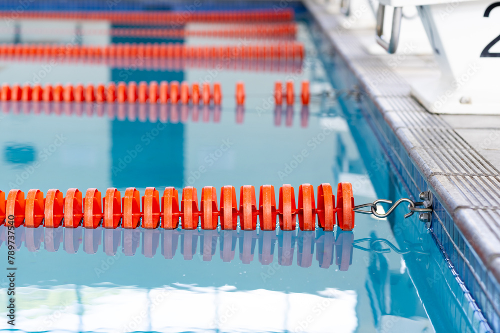 Indoors, orange lane dividers stretch across calm swimming pool water ...
