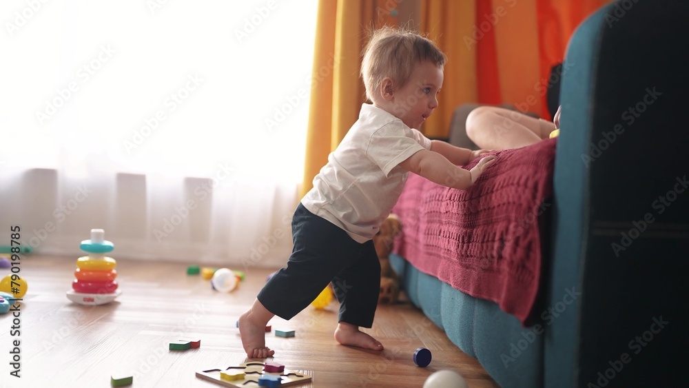 baby tries to get up, takes his a first steps, leans on the sofa. happy ...