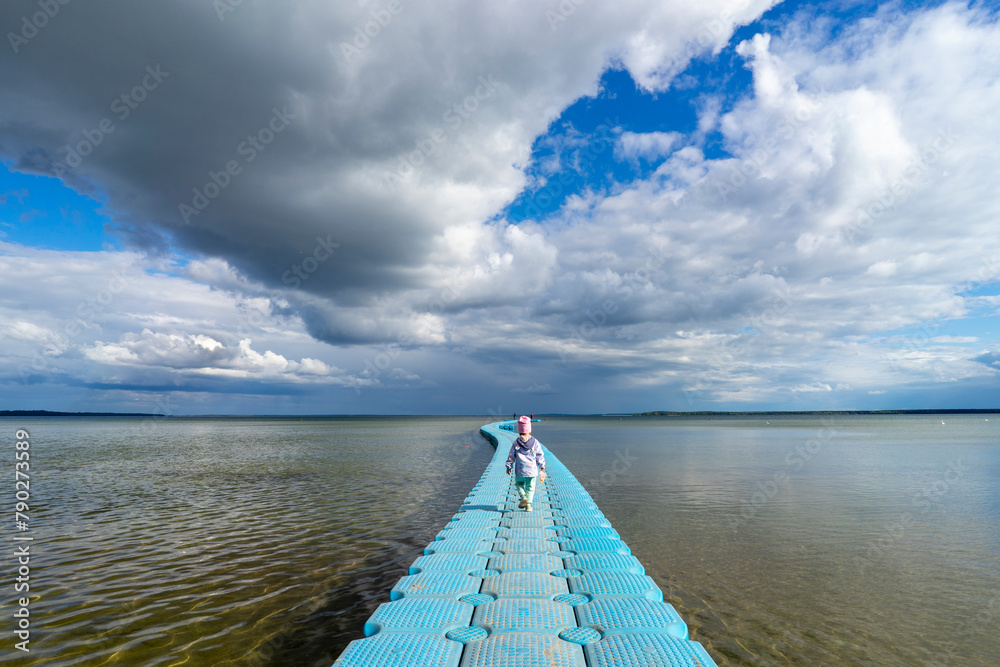 Young girl standing alone on edge of footbridge and staring at lake ...